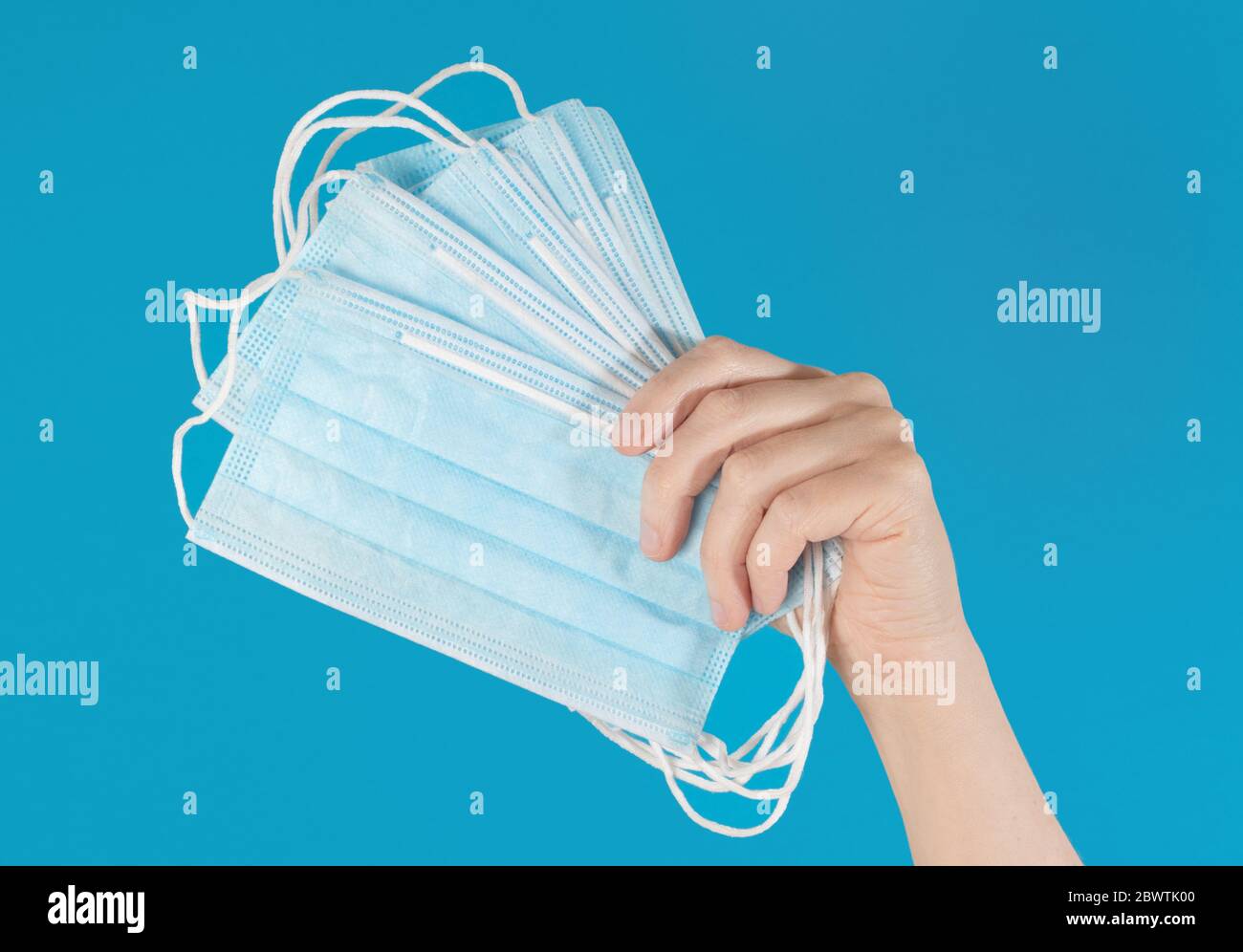 Hand holding up a fan of face masks, isolated against a bright blue ...