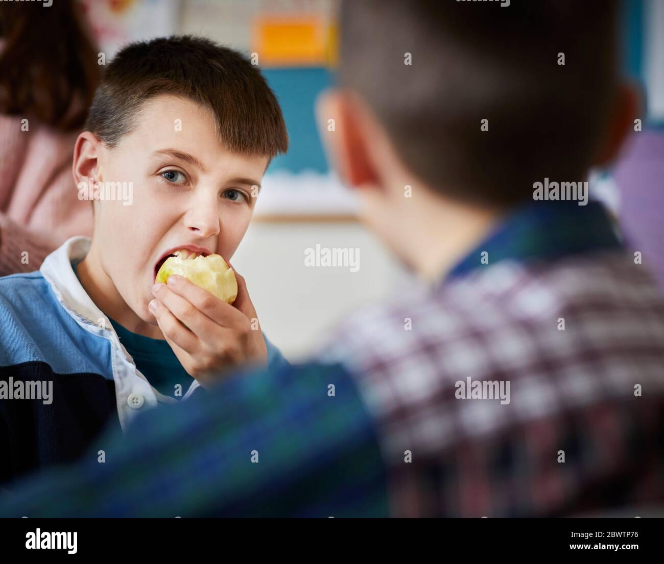 Boy in a classroom during break time eating an apple Stock Photo - Alamy