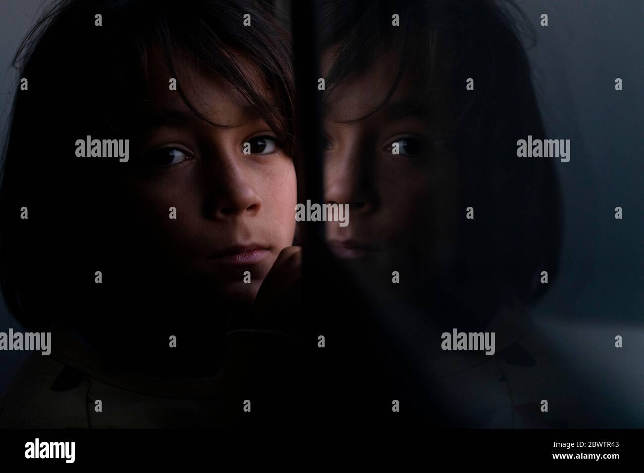 Boy looking at camera at mirrored in window pane at home Stock Photo ...