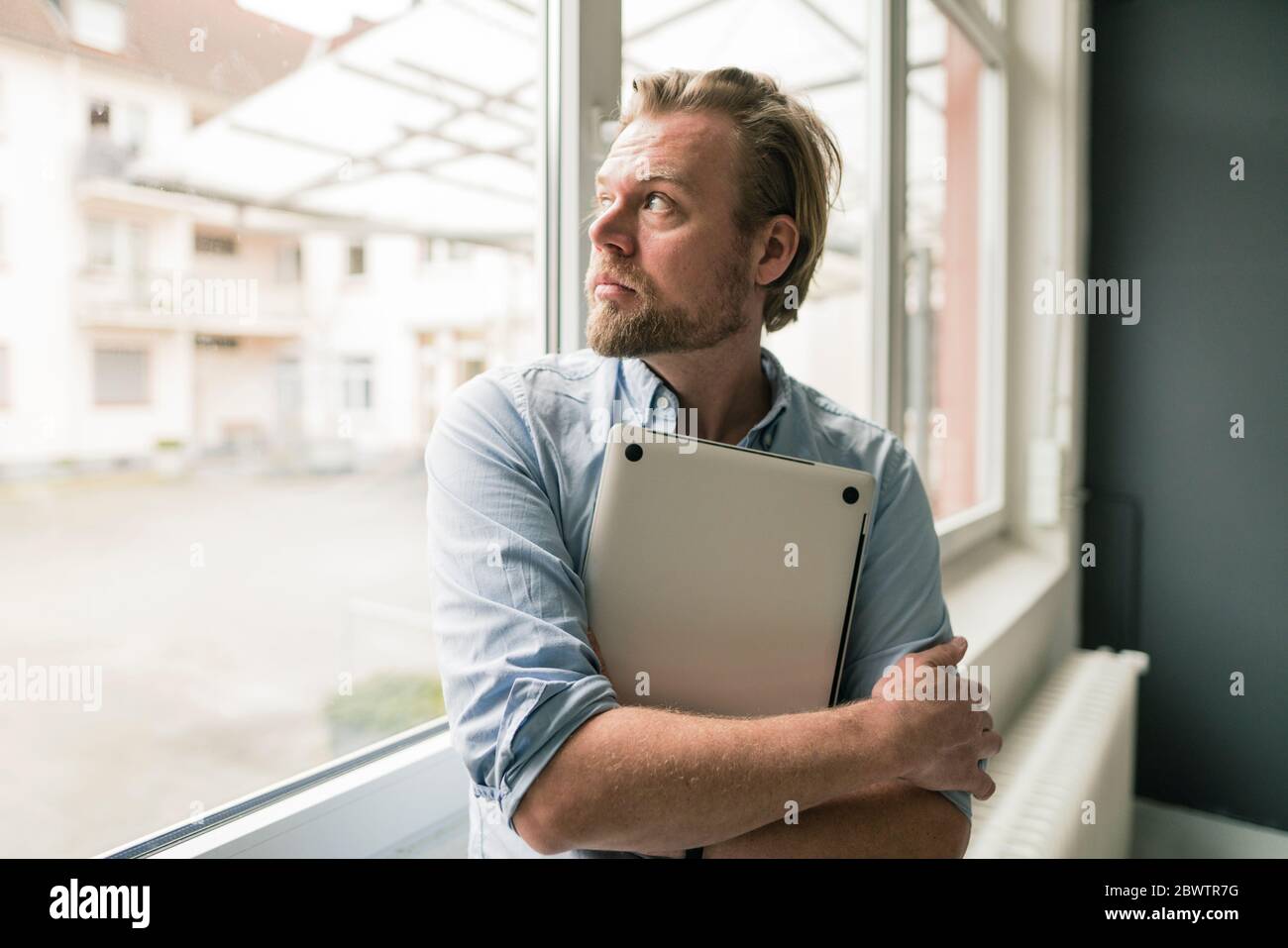 Casual businessman with laptop looking out of window Stock Photo - Alamy