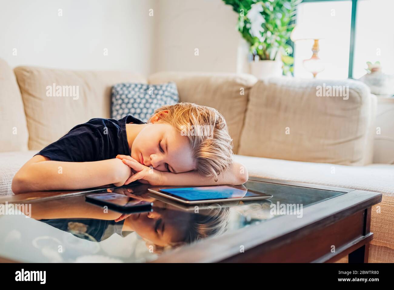 Boy lying on coffee table with smartphone and tablet taking a nap Stock ...