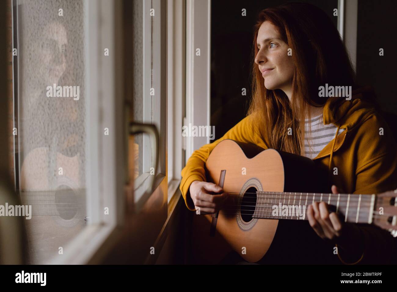 Portrait of relaxed redheaded woman playing guitar at open window Stock ...