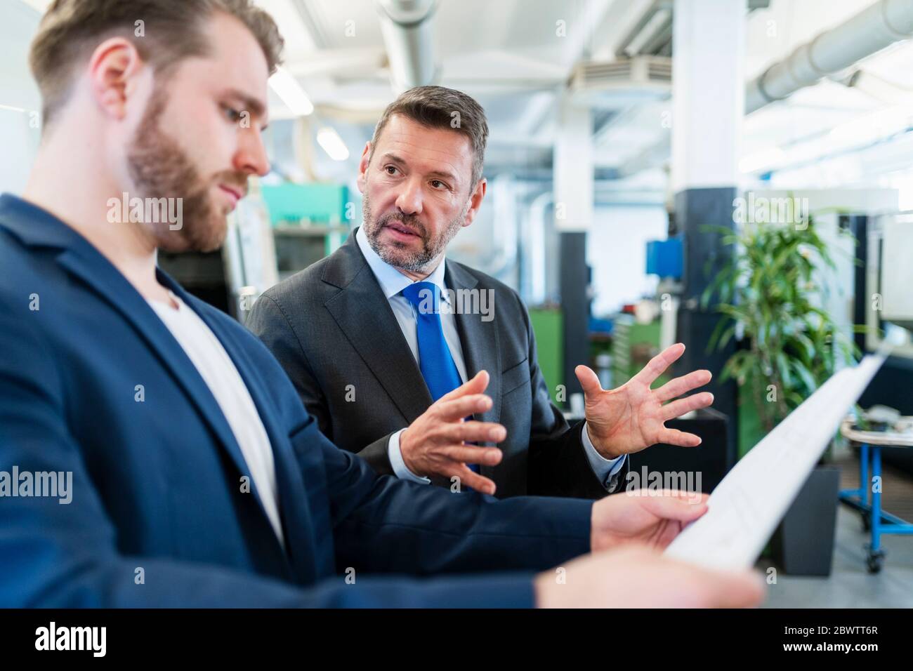 Two businessmen having a work meeting in a factory discussing a plan ...