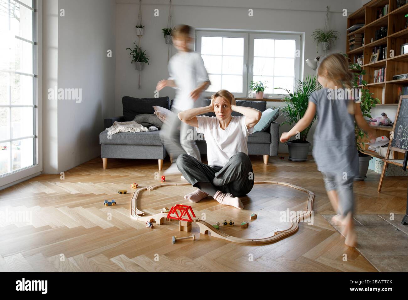 Stressed out mother sitting in the middle of toys, while children are ...