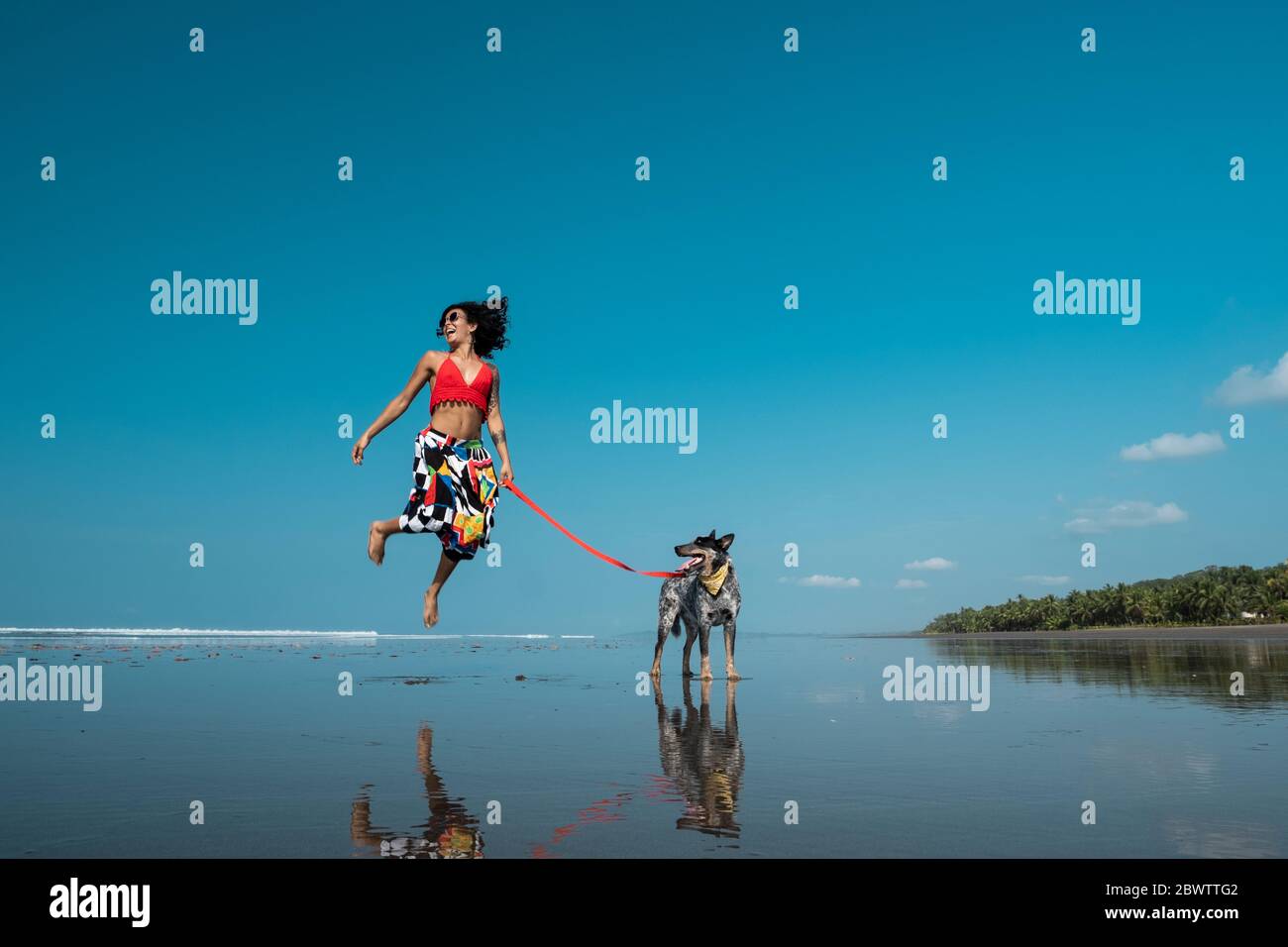 Carefree young woman taking her dog for a walk at the beach, Costa Rica ...