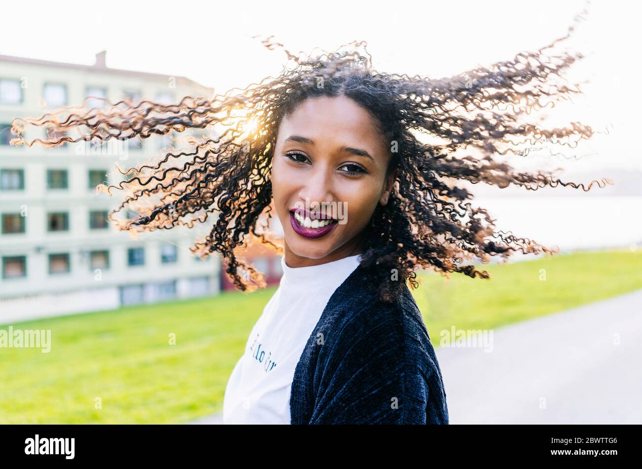 Portrait of young woman with ringlets tossing her hair at backlight ...