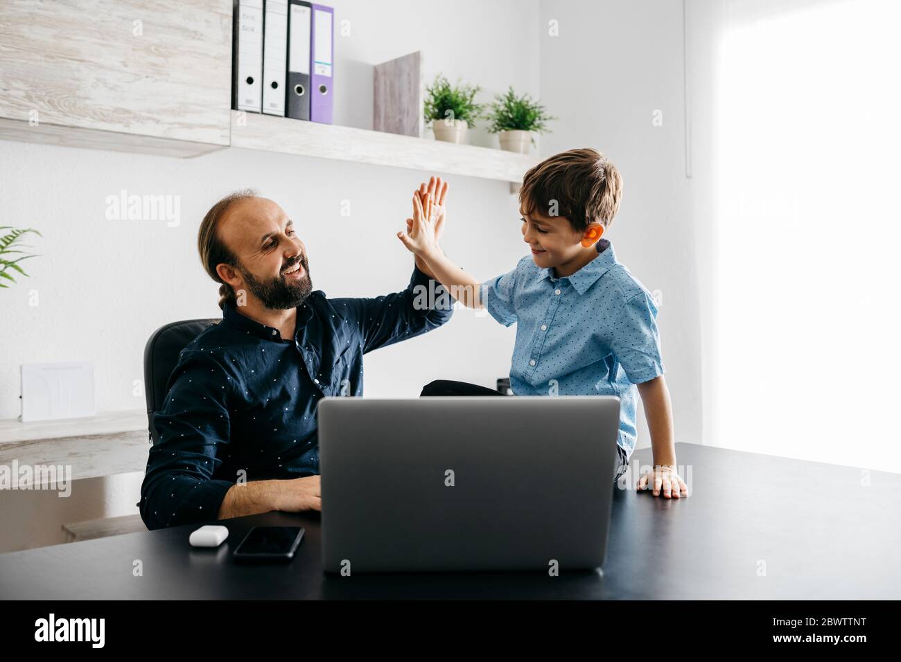 Happy father high fiving with son at desk Stock Photo - Alamy