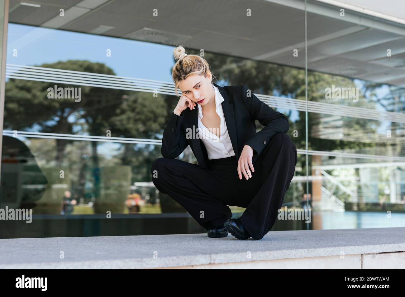 Portrait of young businesswoman wearing black pantsuit crouching in ...