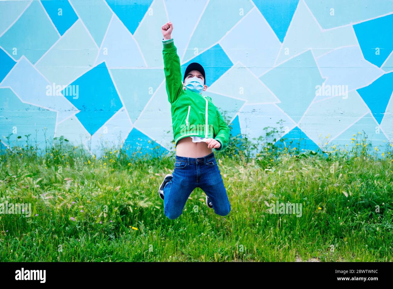 Boy wearing protective mask and jumping on meadow Stock Photo - Alamy