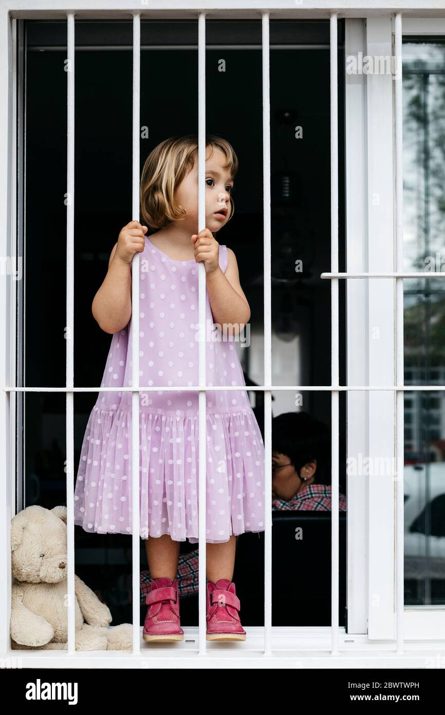 Girl standing at open window looking through window grate Stock Photo ...
