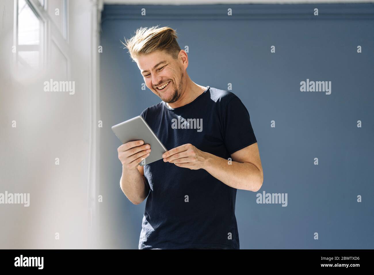 Happy man using a tablet at the window Stock Photo - Alamy
