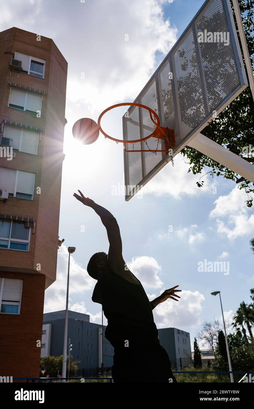 Young man throwing basketball against the sun Stock Photo - Alamy
