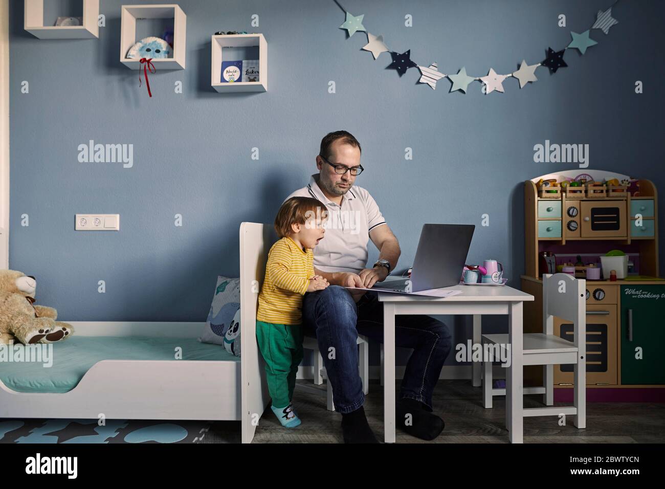 Man working and using laptop in children's room with simultaneous ...
