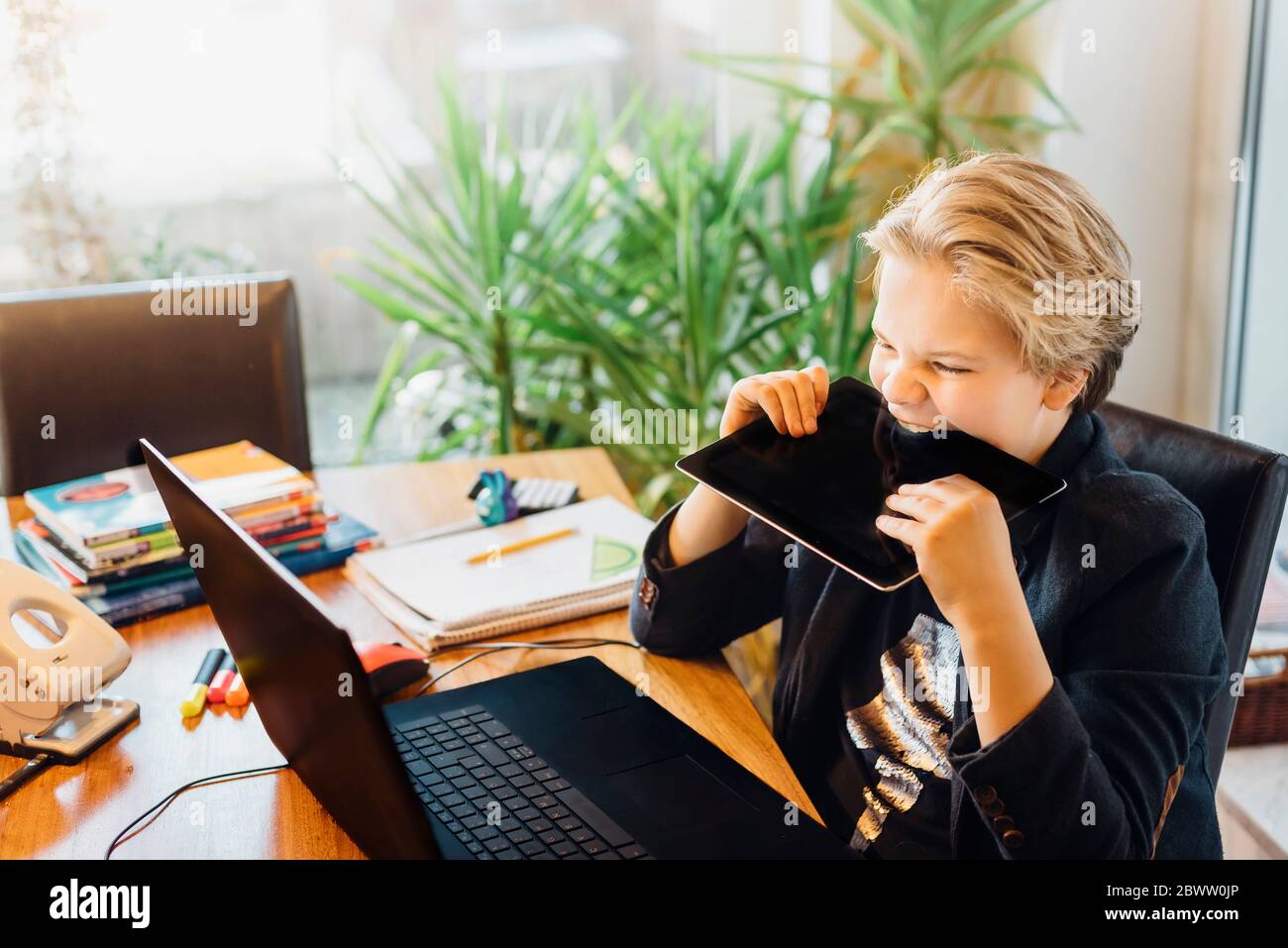 Angry boy sitting at desk biting in tablet Stock Photo - Alamy