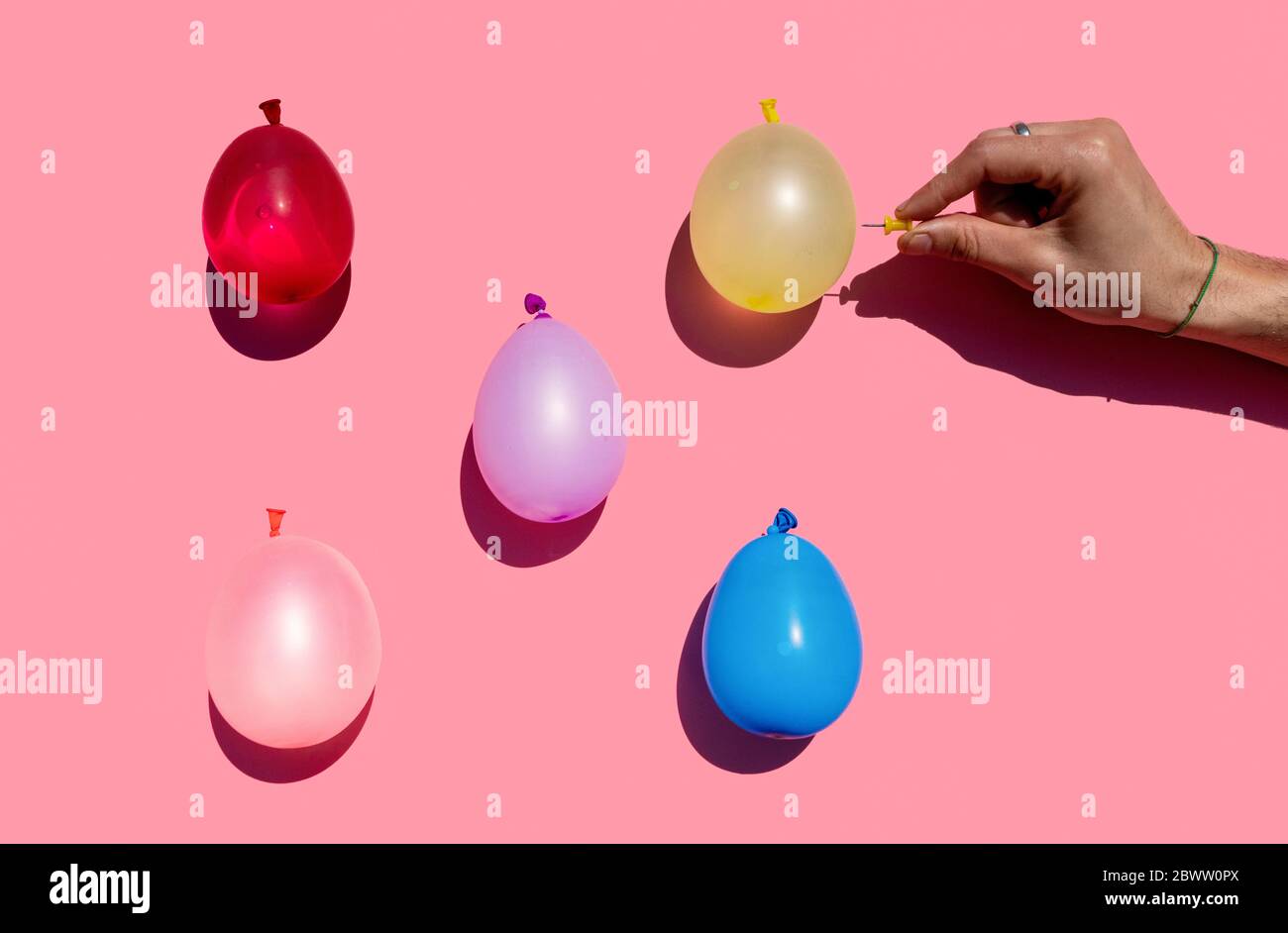Studio shot of hand of man trying to puncture colorful water balloons ...