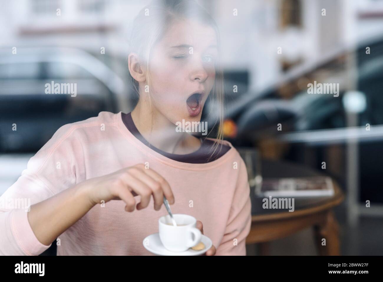 Portrait of young woman grimacing behind windowpane in a cafe Stock ...