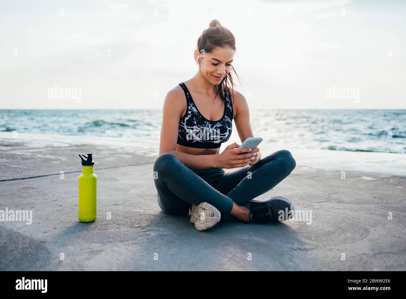 Full length of smiling female athlete using smart phone on promenade ...