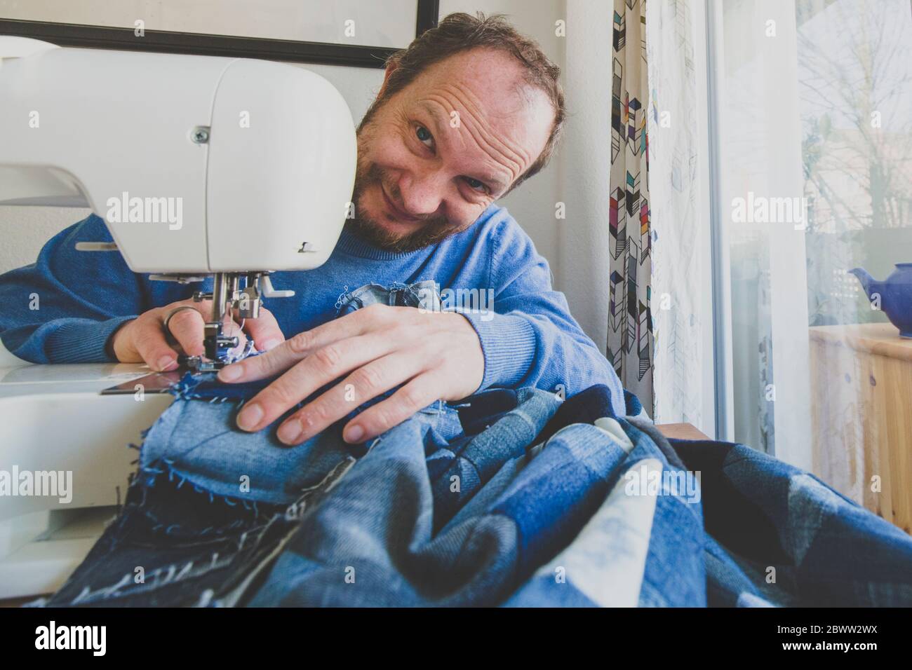 Portrait of smiling man sewing denim quilt at home Stock Photo - Alamy