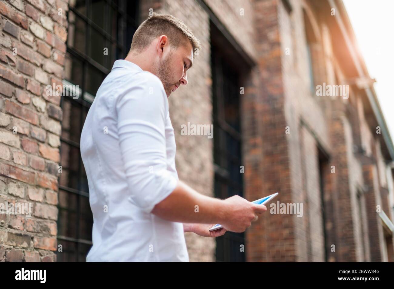 Young businessman using tablet at a brick building Stock Photo - Alamy