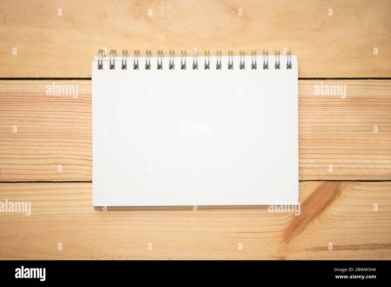 Blank notebook page in the middle of wood office desk table. Top view ...