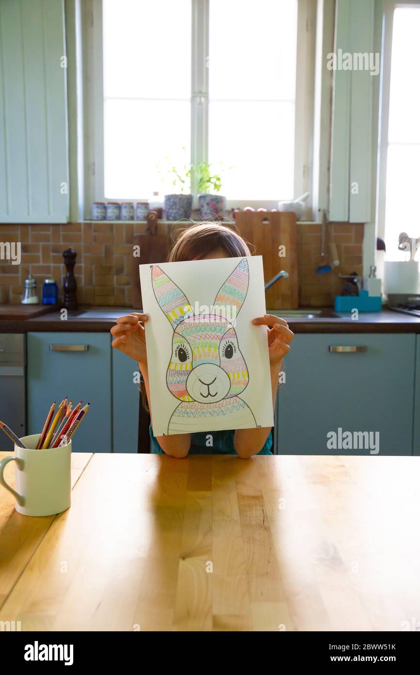 Little girl sitting at kitchen table, holding drawing of Easter bunny ...