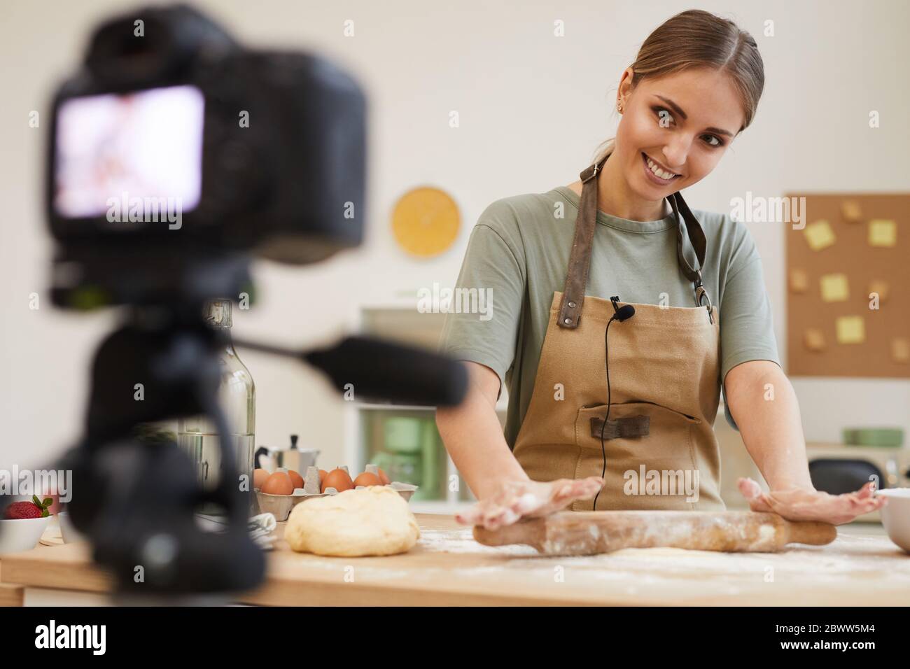 Young woman baking a cake at the table and smiling at camera she ...