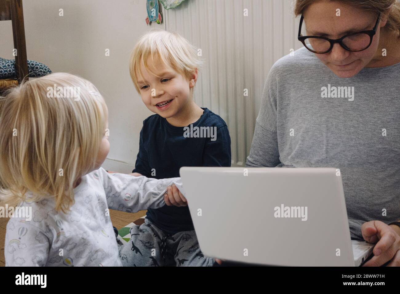 Mother with two little children working on laptop at home Stock Photo ...
