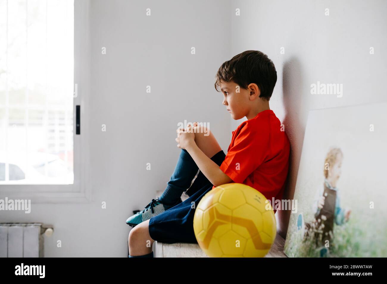 Sad boy with soccer ball sitting on sideboard Stock Photo - Alamy
