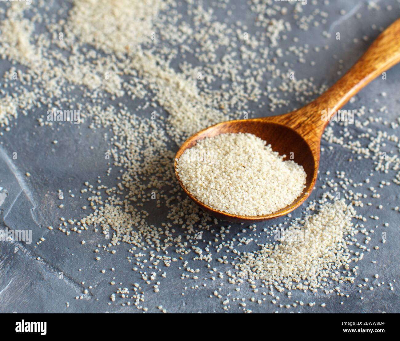 Raw uncooked fonio seeds with a spoon on grey background close up with ...