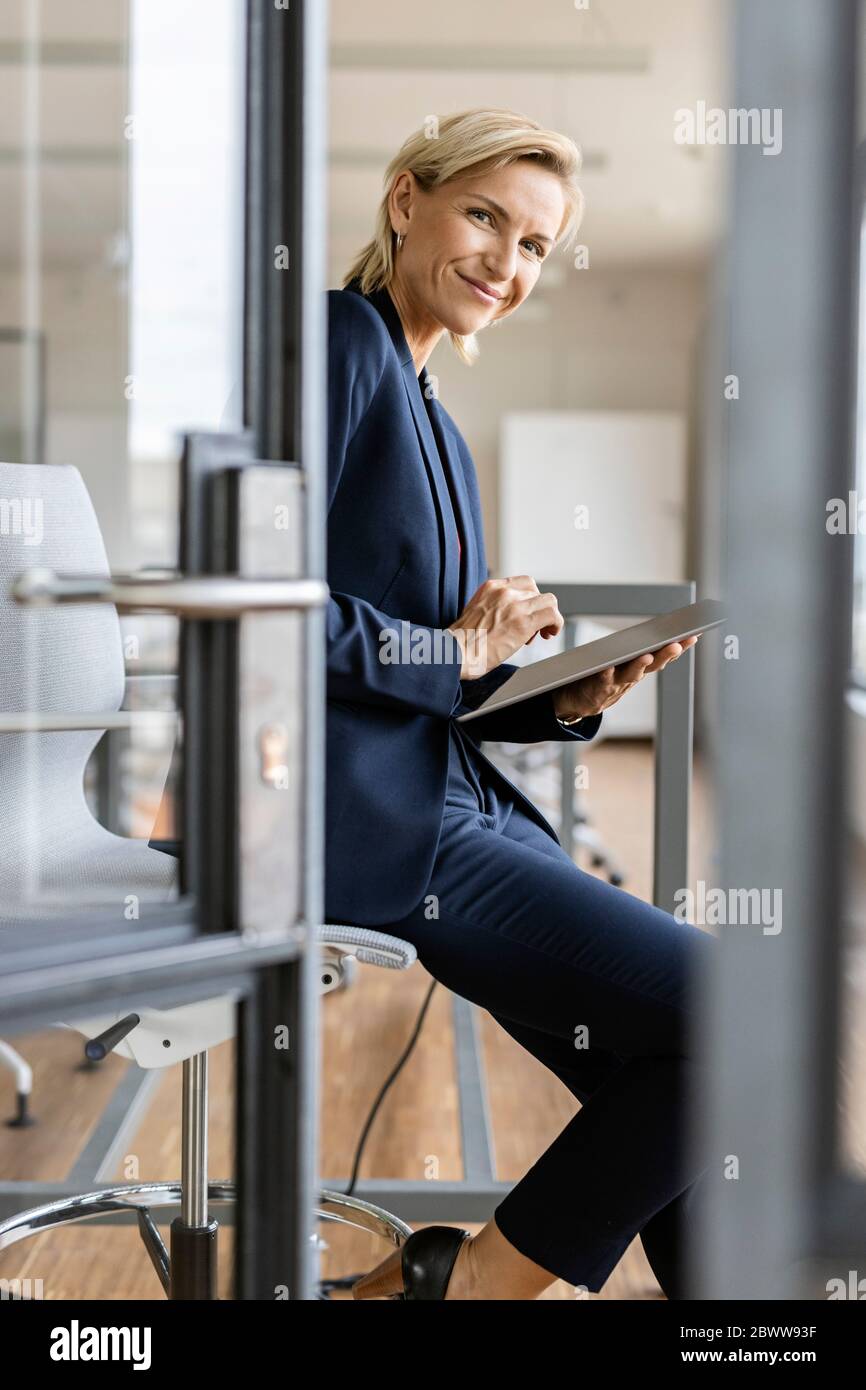 Portrait of smiling blond businesswoman using tablet in conference room ...