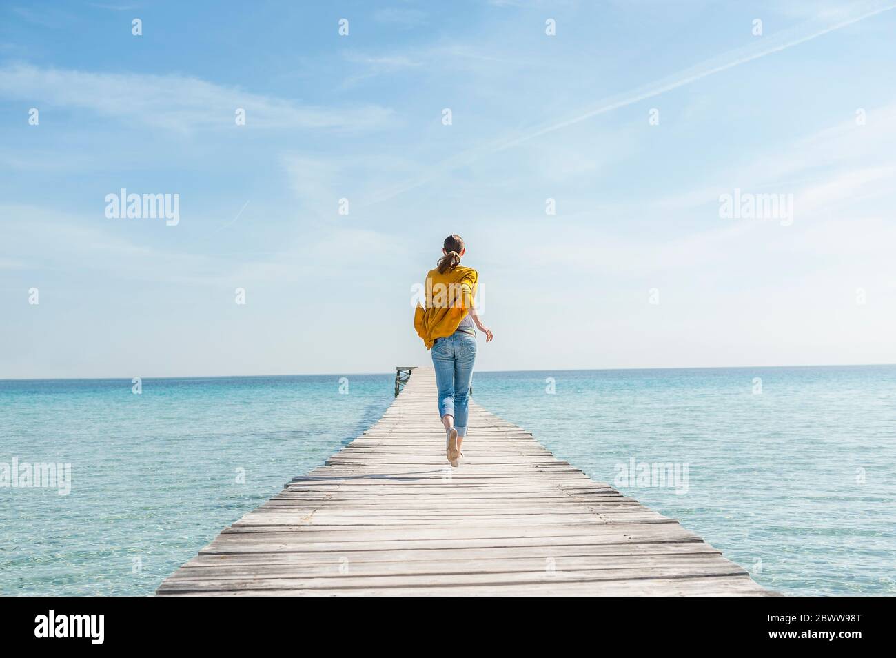 Back view of woman running barefoot on jetty, Mallorca, Spain Stock ...
