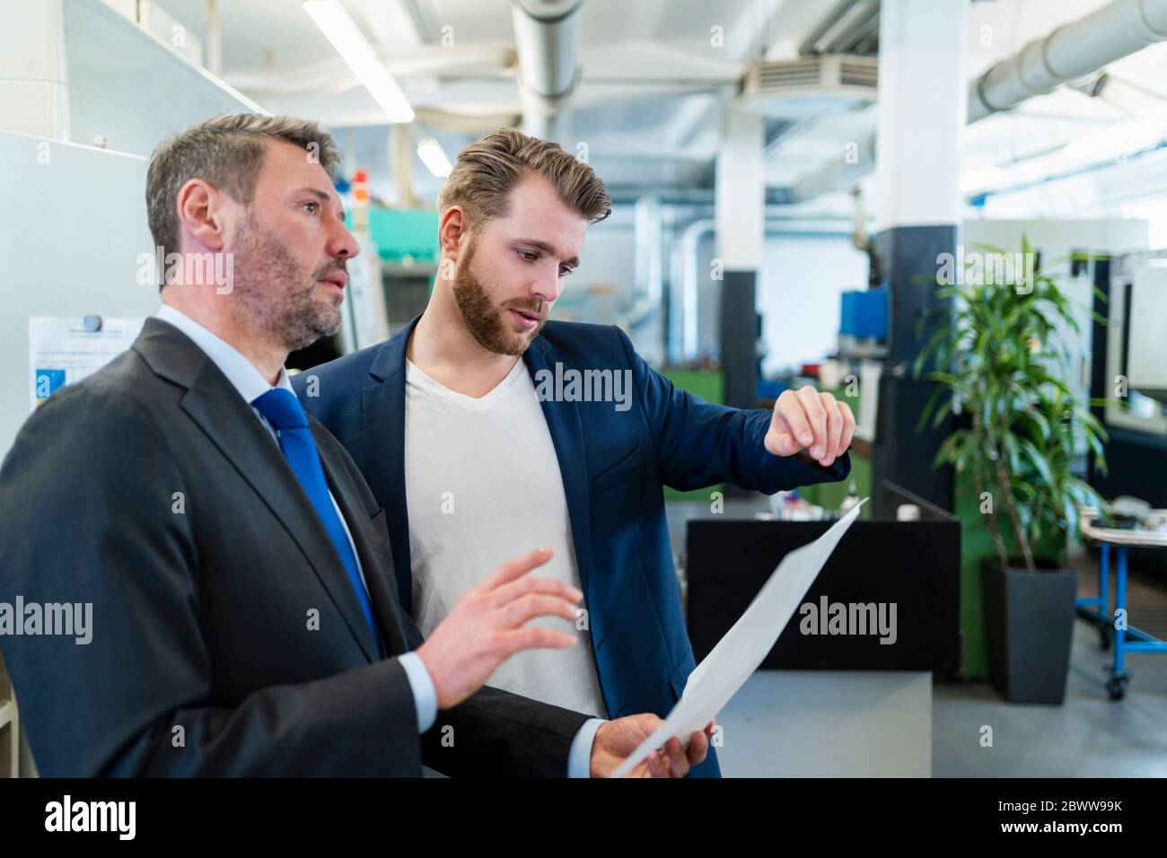 Two businessmen having a work meeting in a factory discussing a plan ...