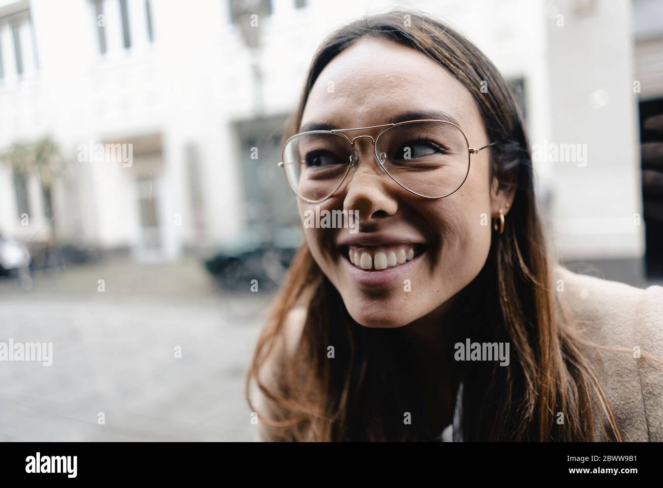 Close-up of smiling woman looking through glass while window shopping ...