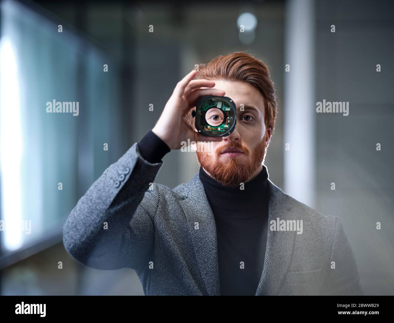 Portrait of businessman looking through an object in modern office ...