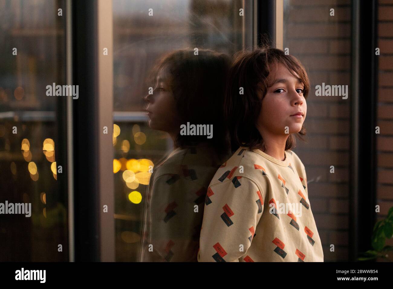 Boy leaning on window, mirrored in glass pane Stock Photo - Alamy