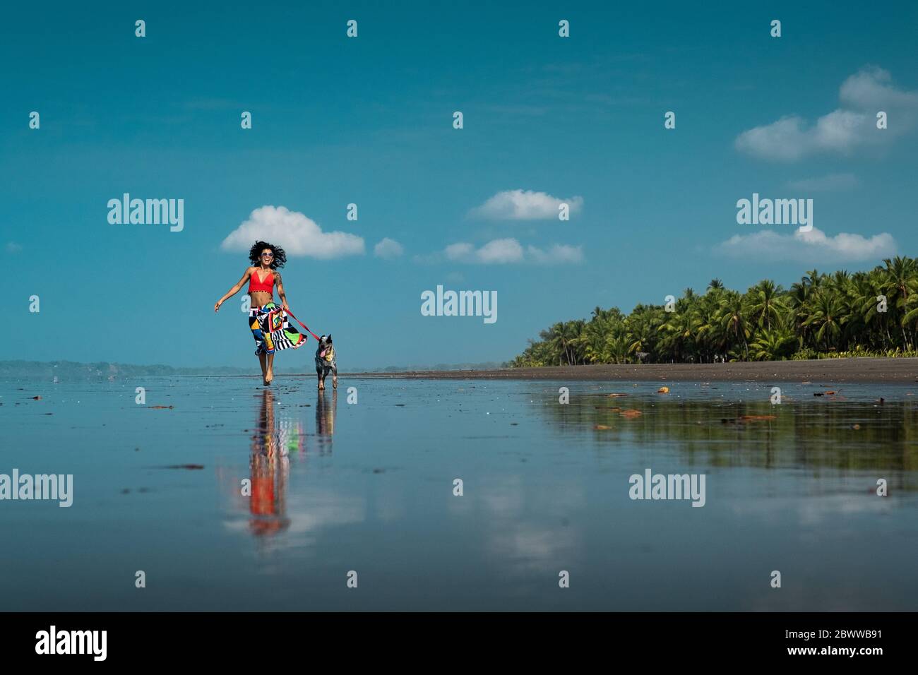 Carefree young woman taking her dog for a walk at the beach, Costa Rica ...