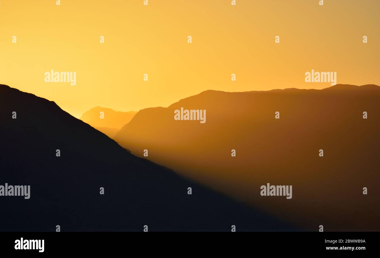Yellow sunset behind black mountains Stock Photo - Alamy