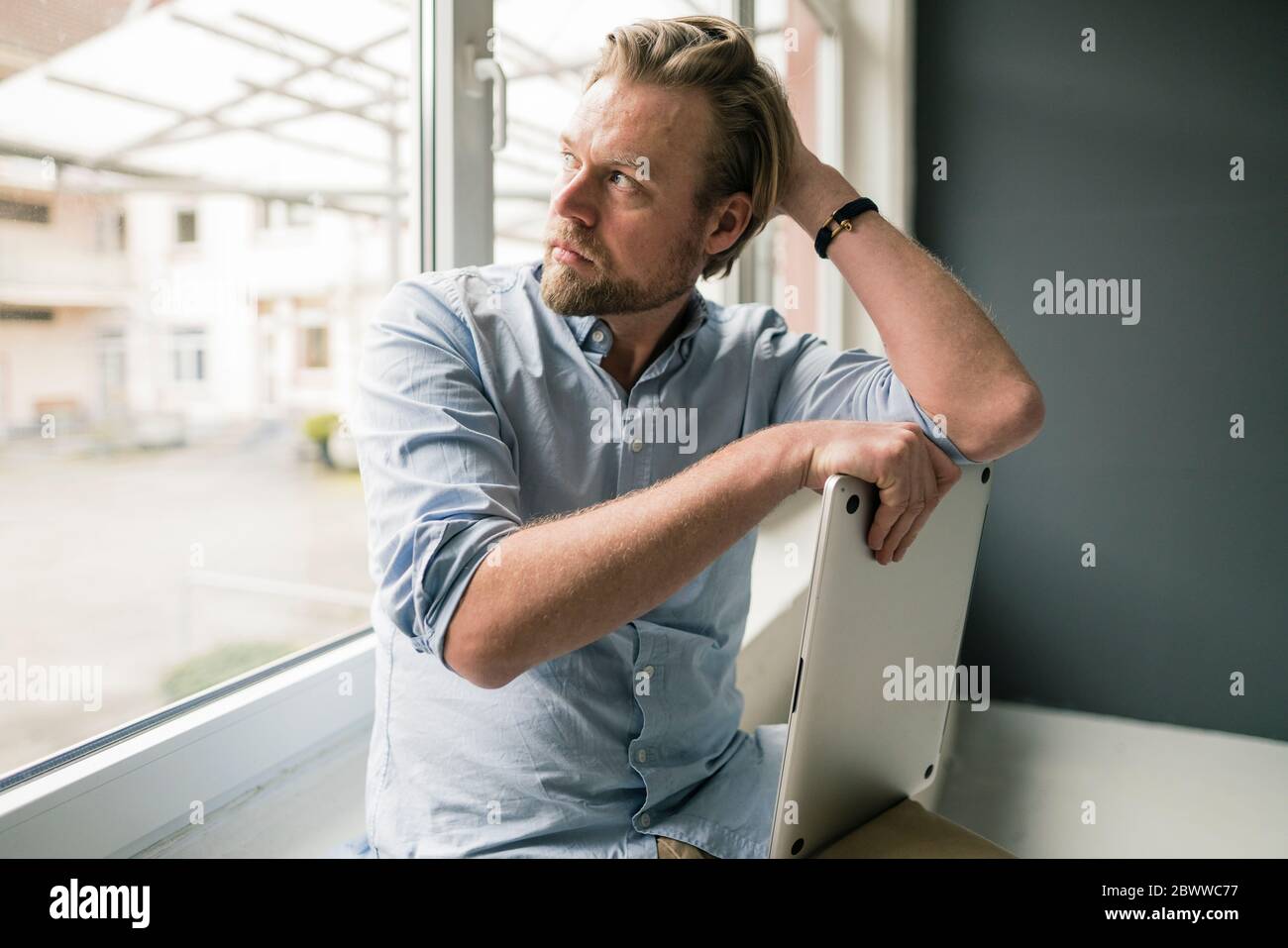 Casual businessman with laptop looking out of window Stock Photo - Alamy