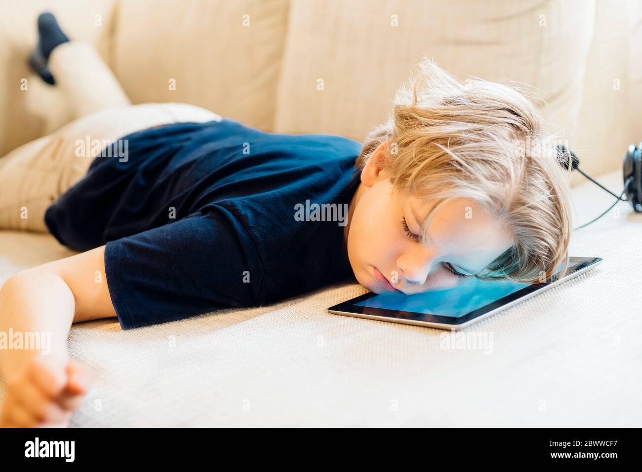 Boy lying on tablet on couch taking a nap Stock Photo - Alamy