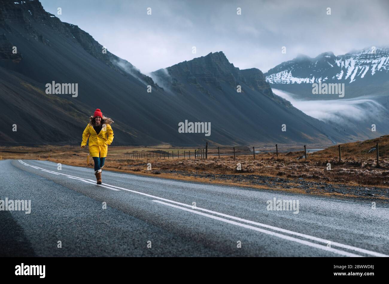 Iceland, Woman in yellow coat running along remote Icelandic highway ...