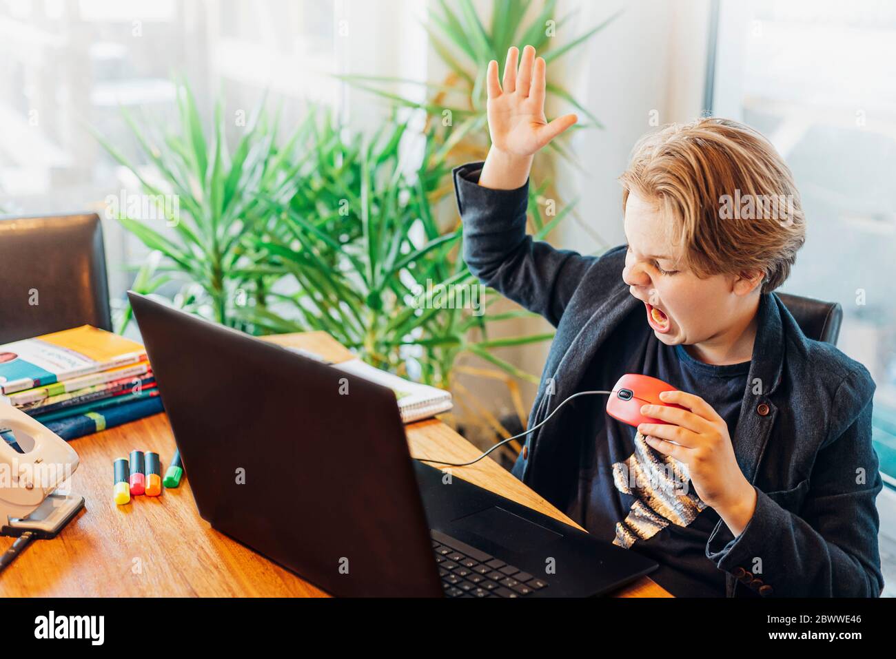 Angry boy sitting at desk with laptop Stock Photo - Alamy