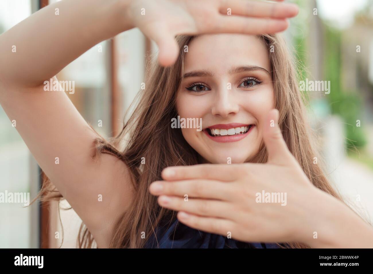Smiling young woman outside in the city framing with hands. Toothy ...