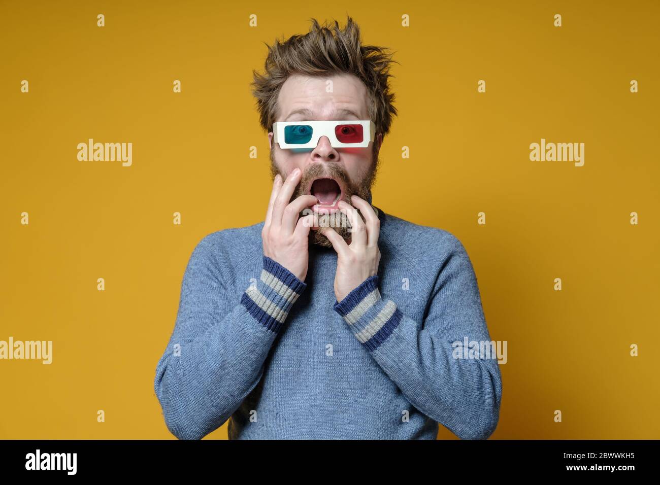 Portrait of a shaggy, bearded scared man in 3D glasses with an open ...