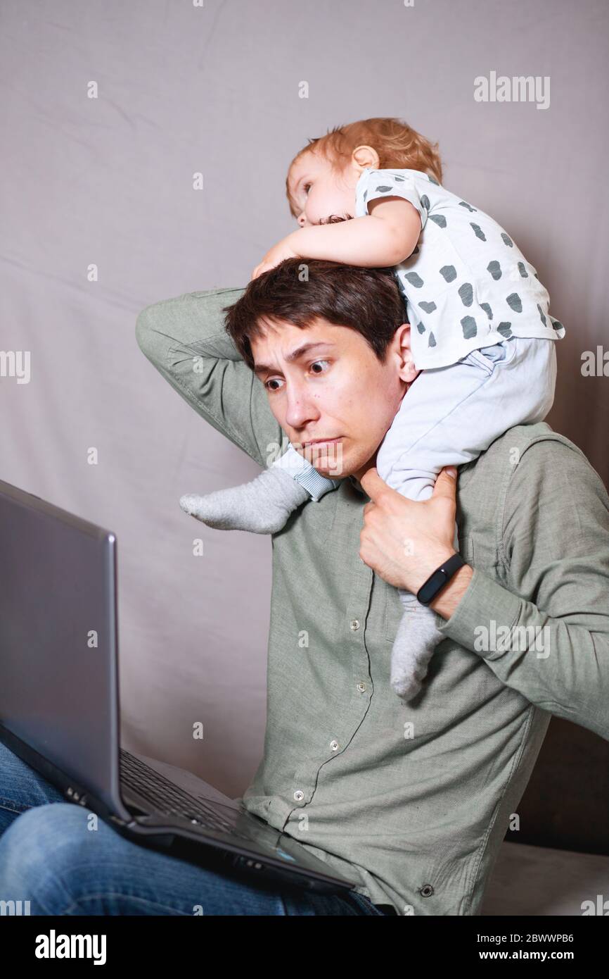 Handsome young man working at home with a laptop with a baby on his ...