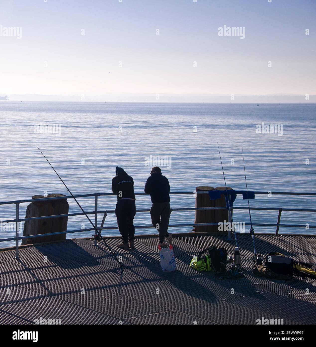 Two men fishing at the end of a pier and looking out to sea Stock Photo ...
