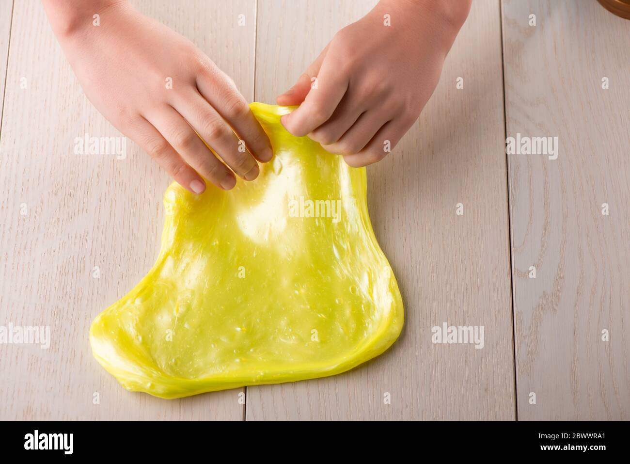 Kid playing with yellow pearlescent slime on wooden table, top view ...