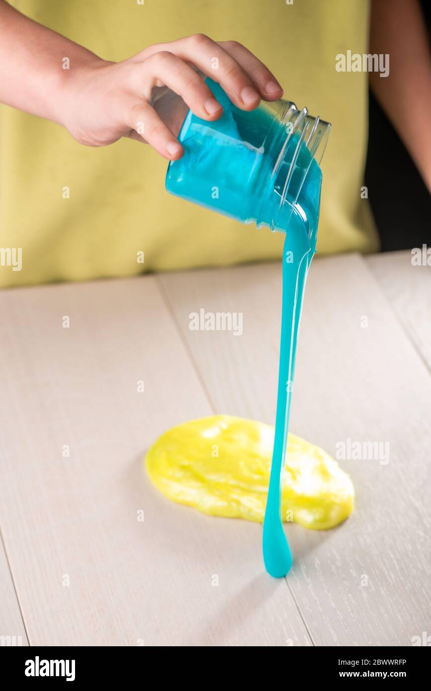 Girl pouring blue slime out of a jar onto a table Stock Photo - Alamy