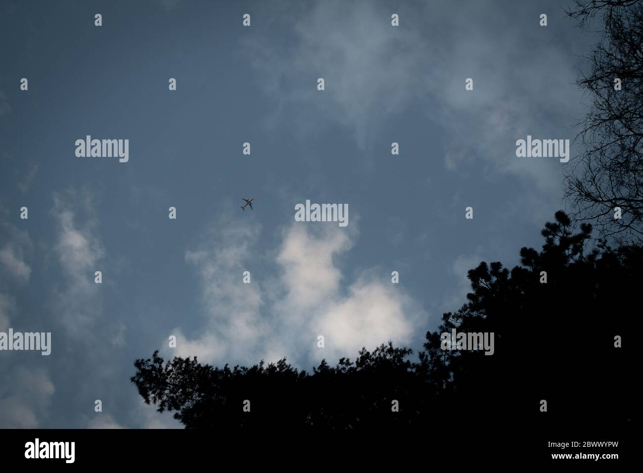 A single plane is crossing the blue sky with some light clouds around ...