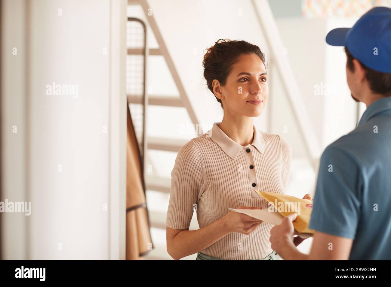 Young woman looking at postman and talking to him while delivering ...