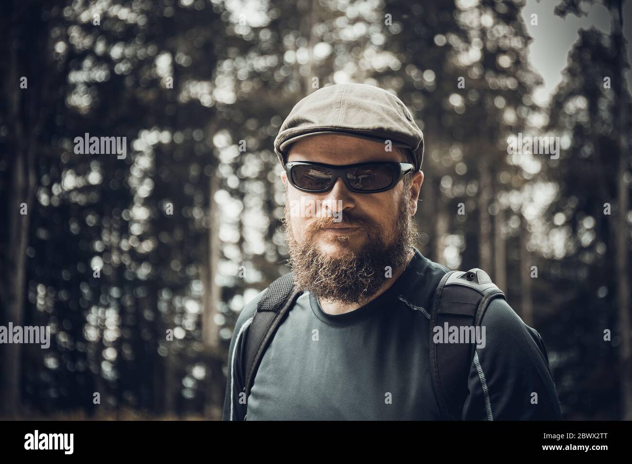 Solid bearded man in sunglasses and cap portrait on forest background ...